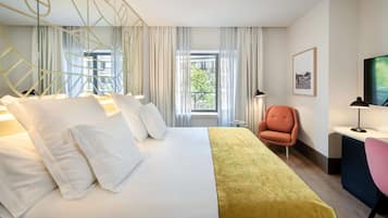 Quarto de hotel com uma cama grande, uma mesa de trabalho com cadeira, televisão e uma janela com cortinas.