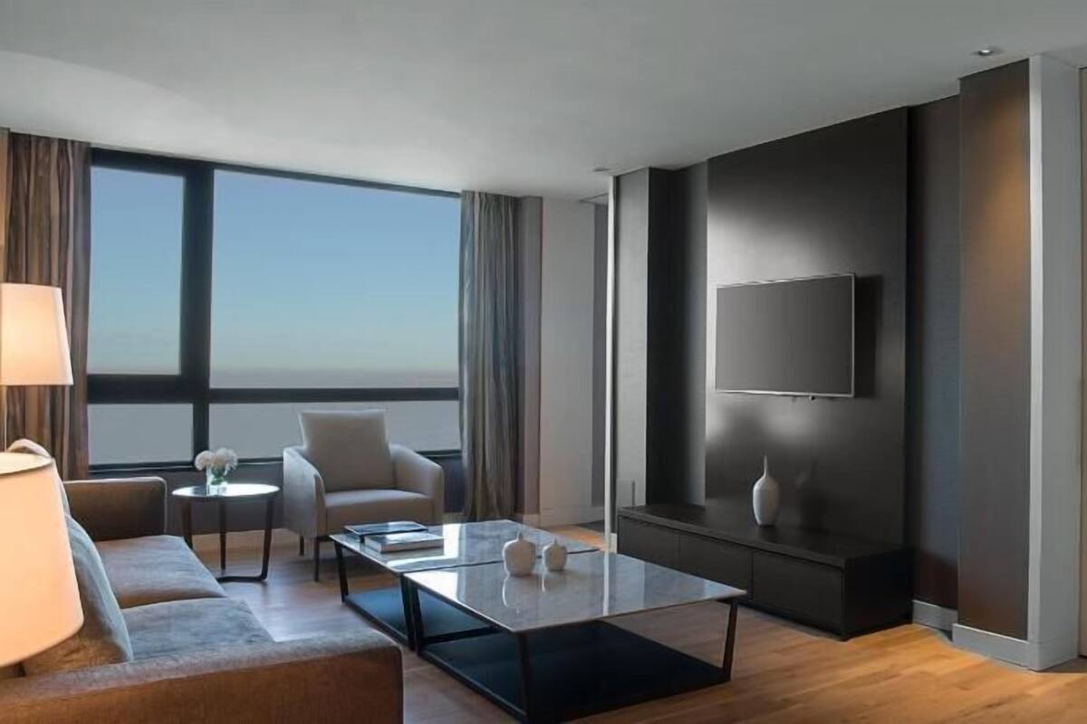 Quarto de hotel moderno com sofá, mesa de centro, televisão fixada na parede e uma cama.