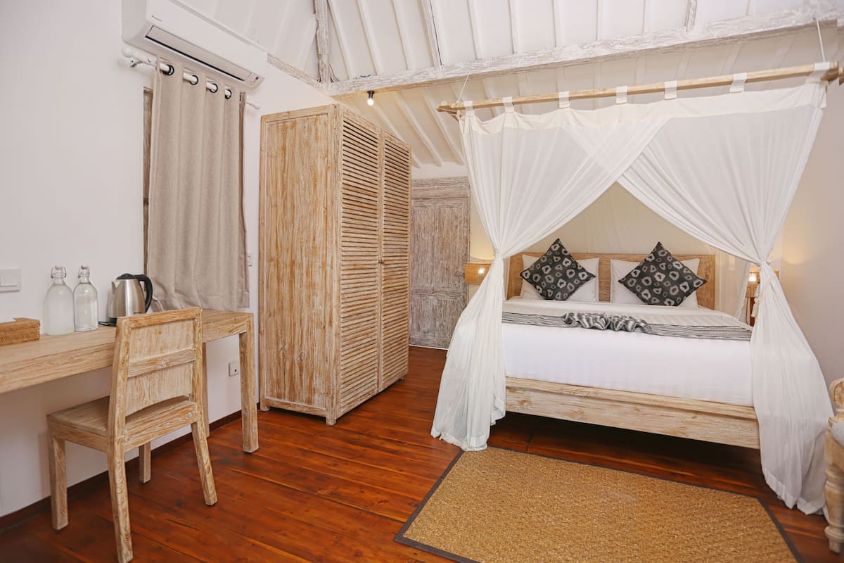 Quarto com cama de madeira, dossel branco e escrivaninha com cadeira.