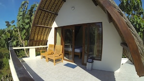 Uma casa moderna com telhado inclinado, grandes portas de vidro e um alpendre com duas cadeiras de madeira.