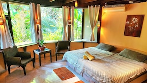 Quarto com cama, duas cadeiras, uma mesinha com planta em vaso e janela com cortinas.