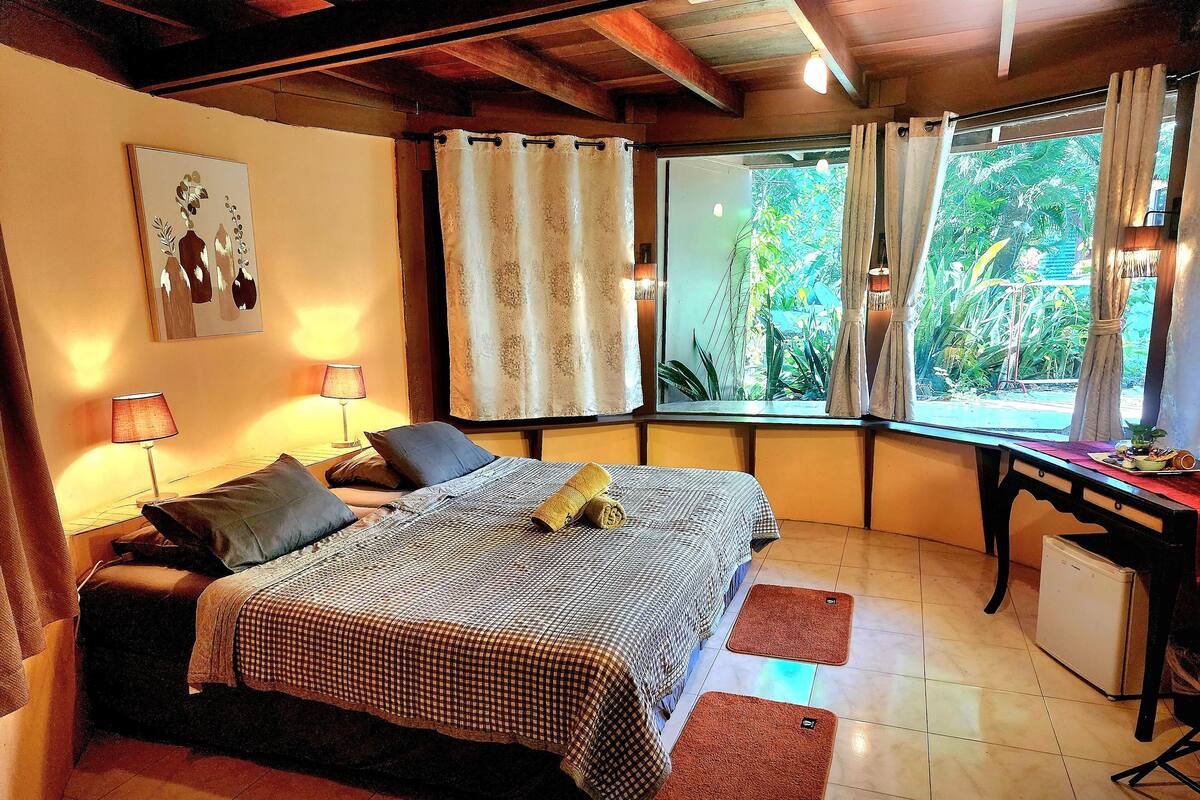 Quarto com cama, abajures, escrivaninha e janela com cortinas.