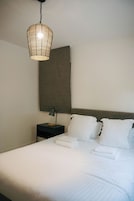 Quarto de hotel com uma cama bem arrumada, mesa de cabeceira com abajur e luminária suspensa.