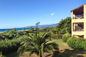 Um edifício com varanda que dá para um jardim com palmeiras e vista para o mar e as montanhas.