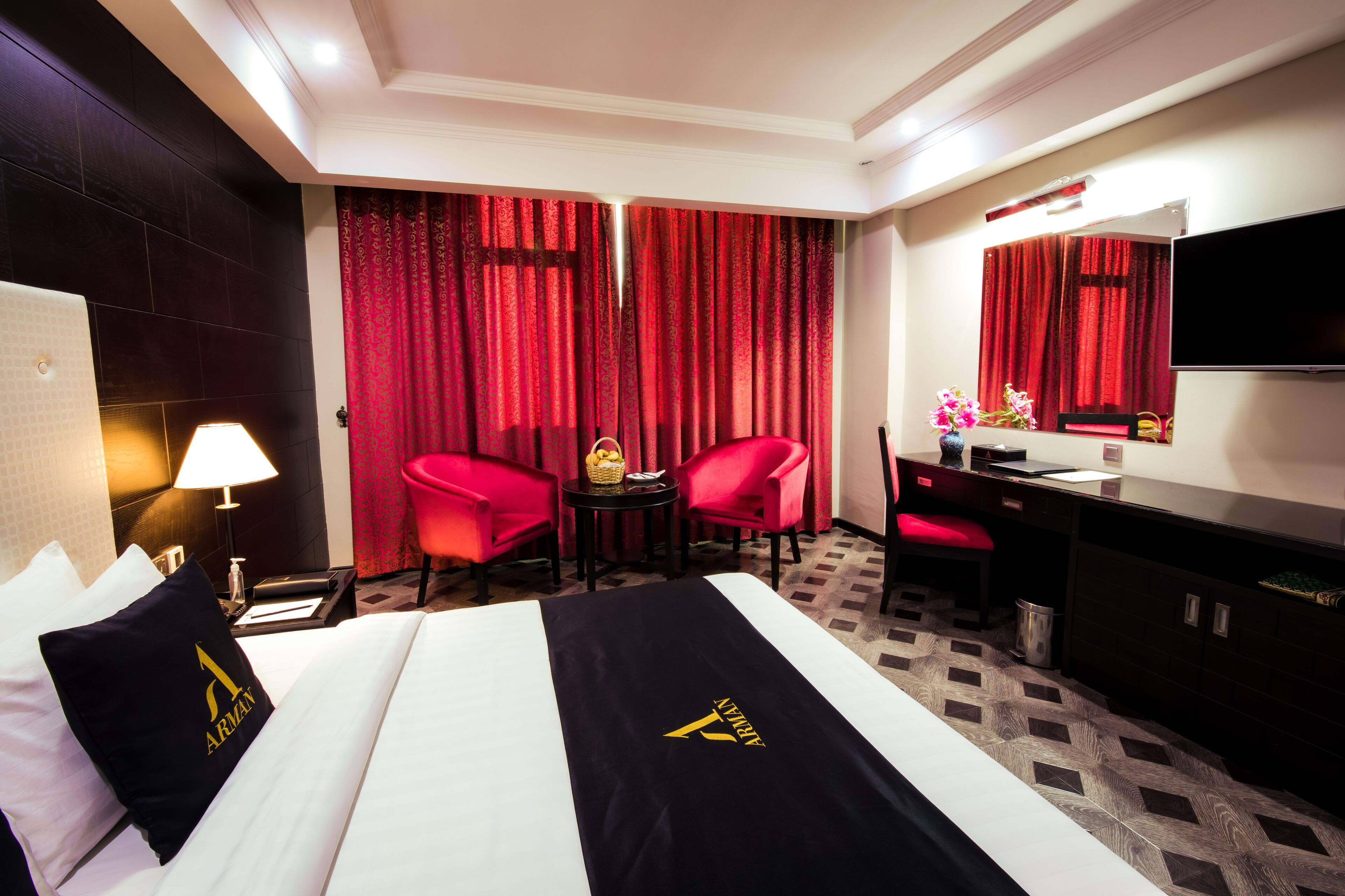 Quarto de hotel com uma cama, uma escrivaninha, uma cadeira, uma televisão e uma cortina vermelha.