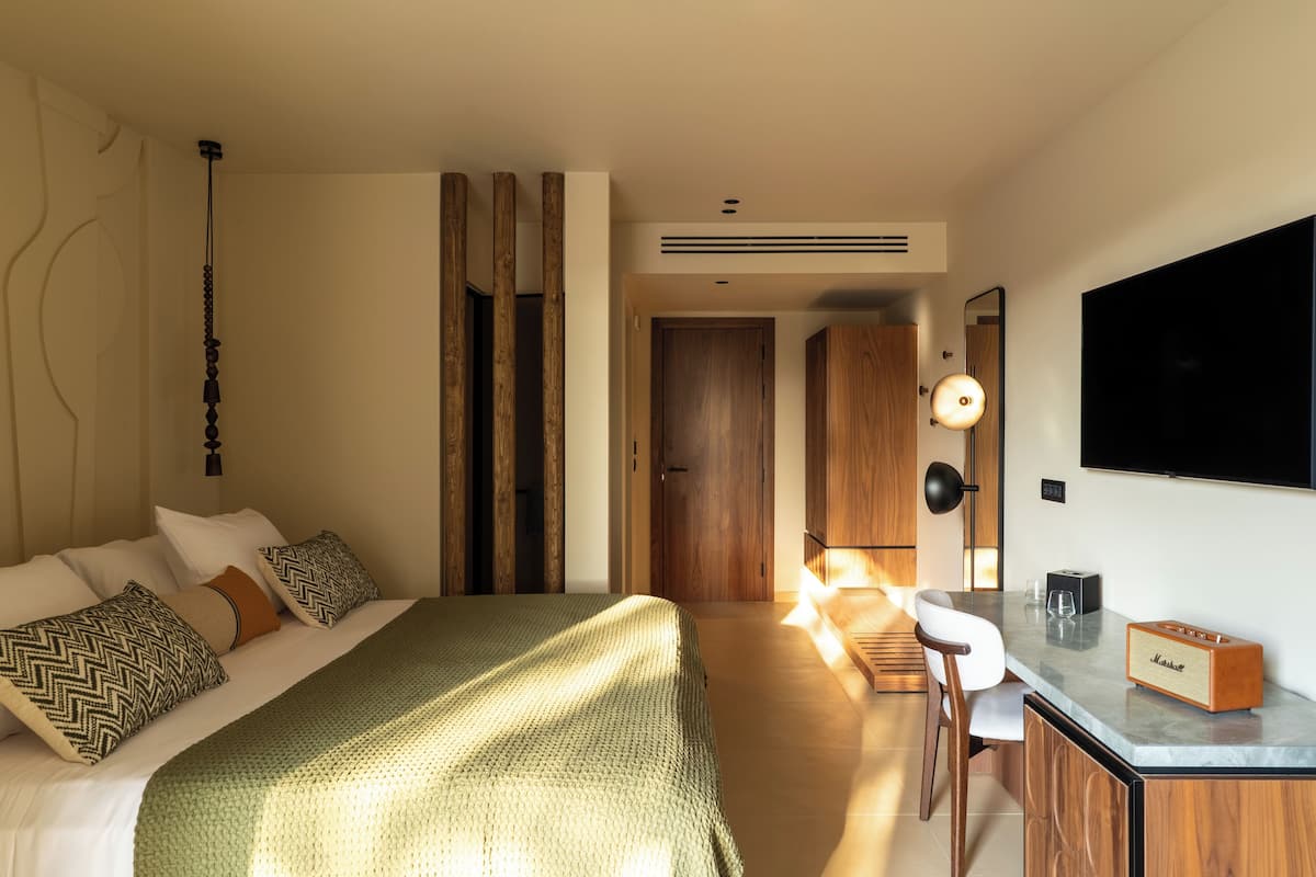 Quarto de hotel moderno com cama, escrivaninha, cadeira, TV e minibar.
