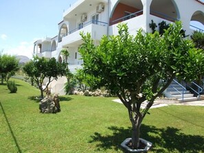 Edifício branco com várias varandas e um jardim bem cuidado com árvores.