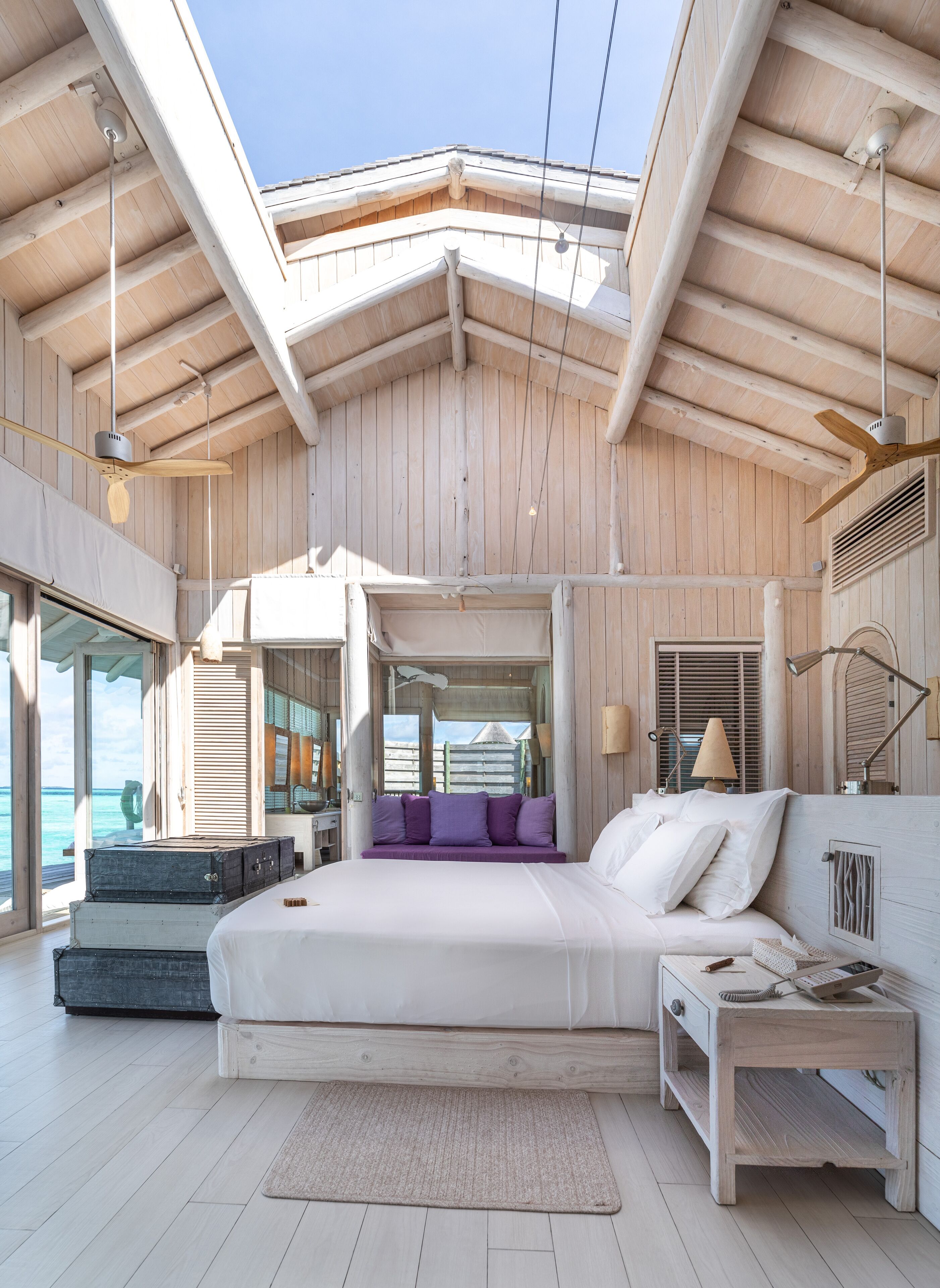 Um quarto espaçoso com uma cama grande, teto de madeira e vista para o mar.