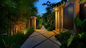 Um caminho leva a um edifício de design moderno, cercado por vegetação exuberante e iluminado por luz quente.