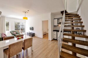 Um apartamento moderno com escada de madeira, área de jantar com mesa e cadeiras brancas e cozinha com armários brancos.