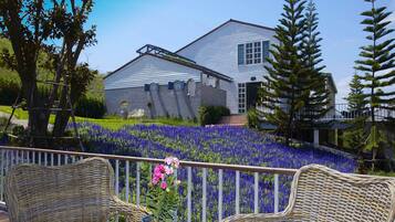 Uma casa com varanda e vista para um jardim com flores roxas.