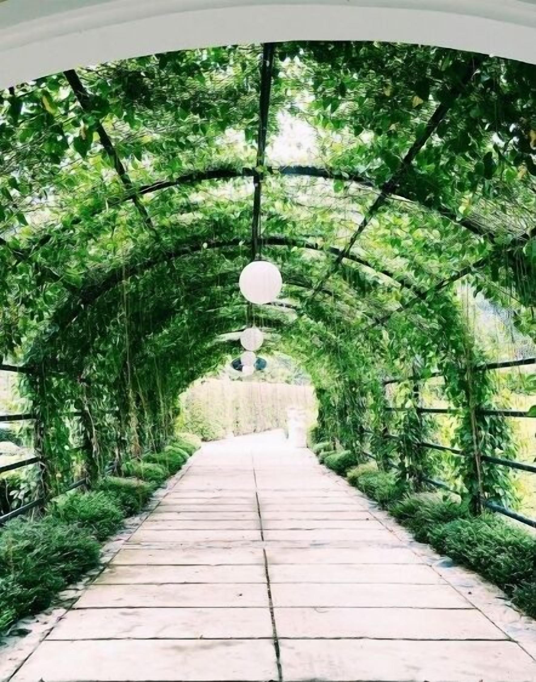 Um caminho sob um arco verde com decorações esféricas penduradas.