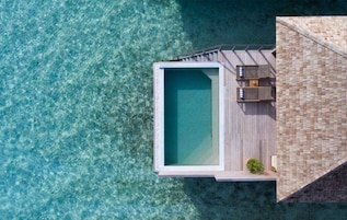 Vista aérea de uma piscina infinita moderna com deck de madeira e área de estar.