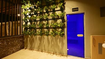 Paredes com plantas em vasos, uma porta azul e um letreiro indicando uma sala de vapor.