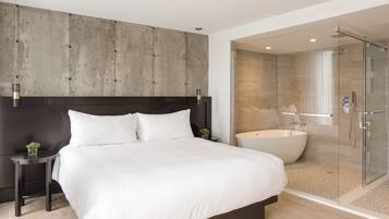 Quarto de hotel moderno com uma cama grande, mesa de cabeceira, chuveiro com divisória de vidro e banheira.