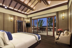 Quarto de hotel com cama grande, televisão, varanda com mesa e cadeiras, e vista para o exterior.