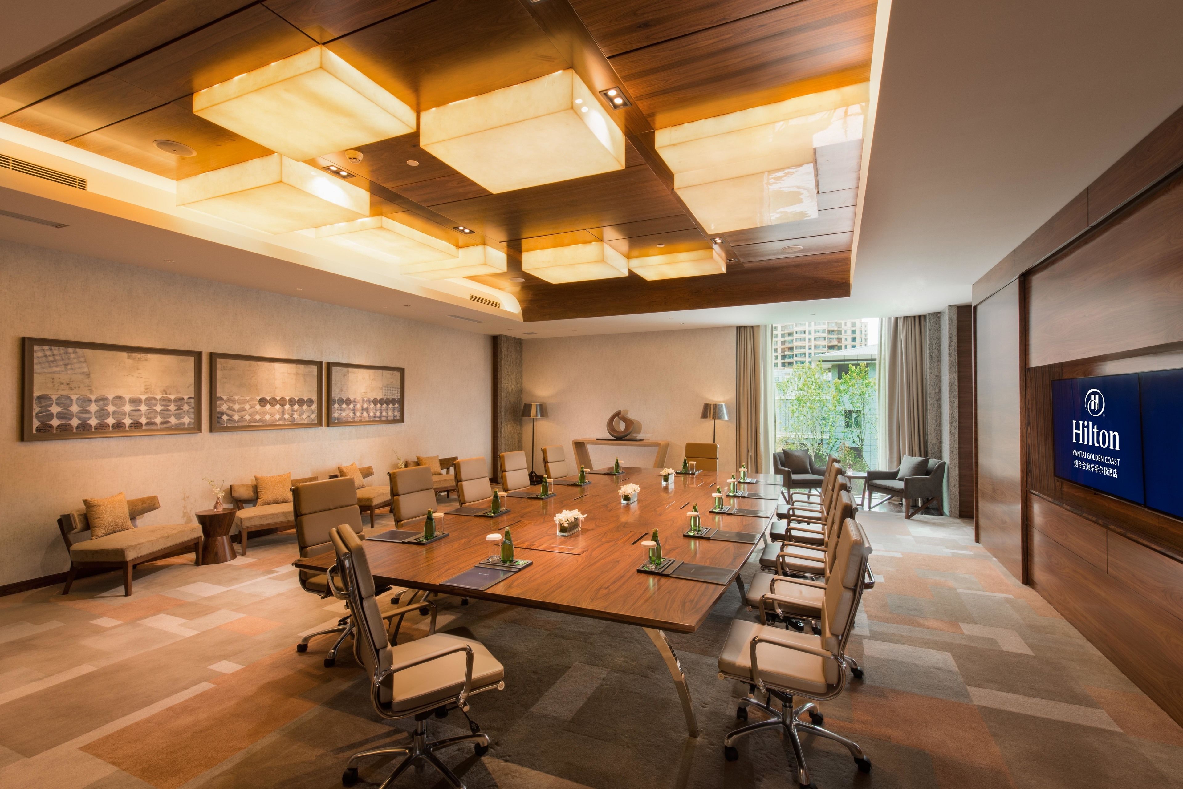 Uma sala de conferências com uma mesa comprida, cadeiras e uma tela de televisão exibindo o logotipo da Hilton.