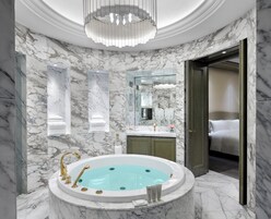 Um banheiro luxuoso com piso de mármore, uma banheira livremente posicionada, um espelho grande e um candelabro.