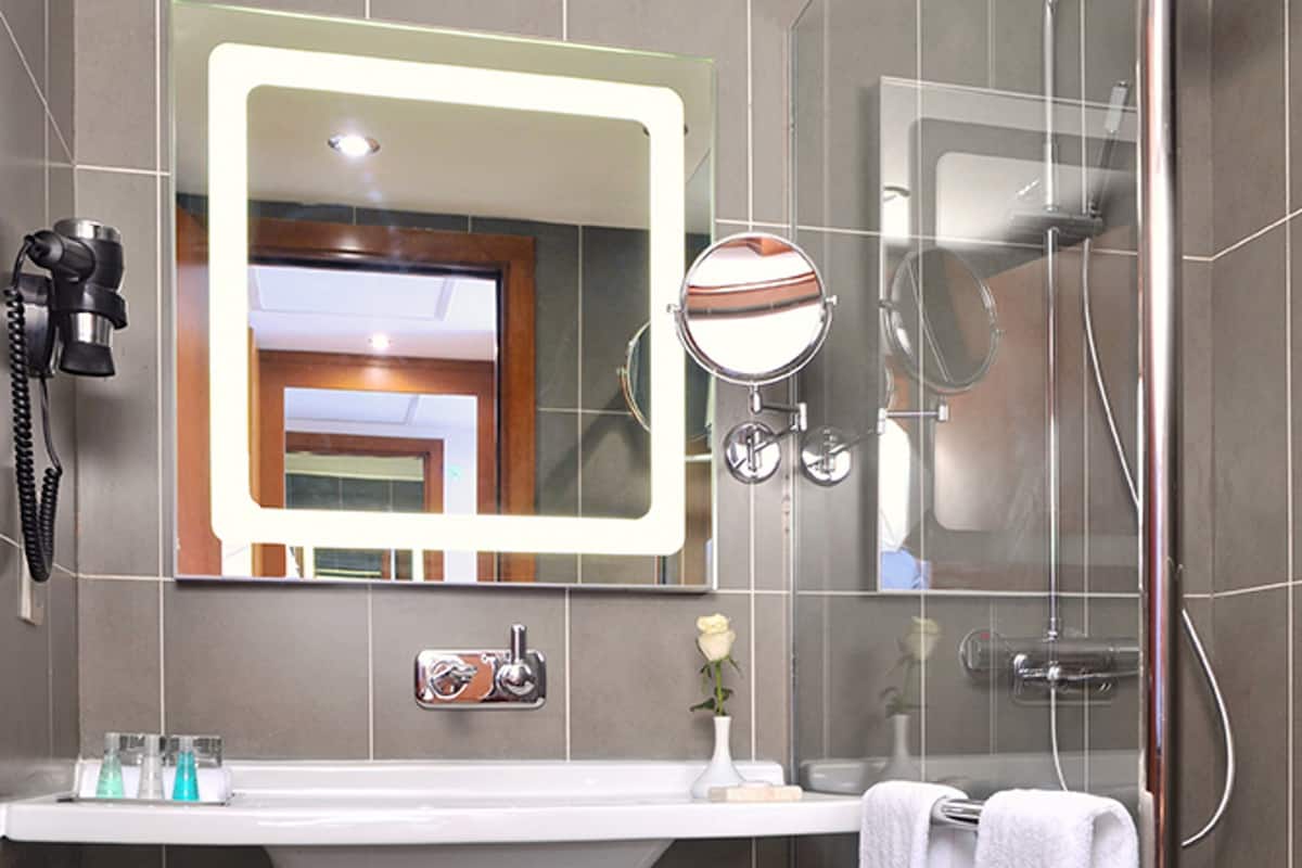Casa de banho moderna com um espelho grande, um secador de cabelo, um espelho redondo, chuveiro e lavatório com produtos de higiene.