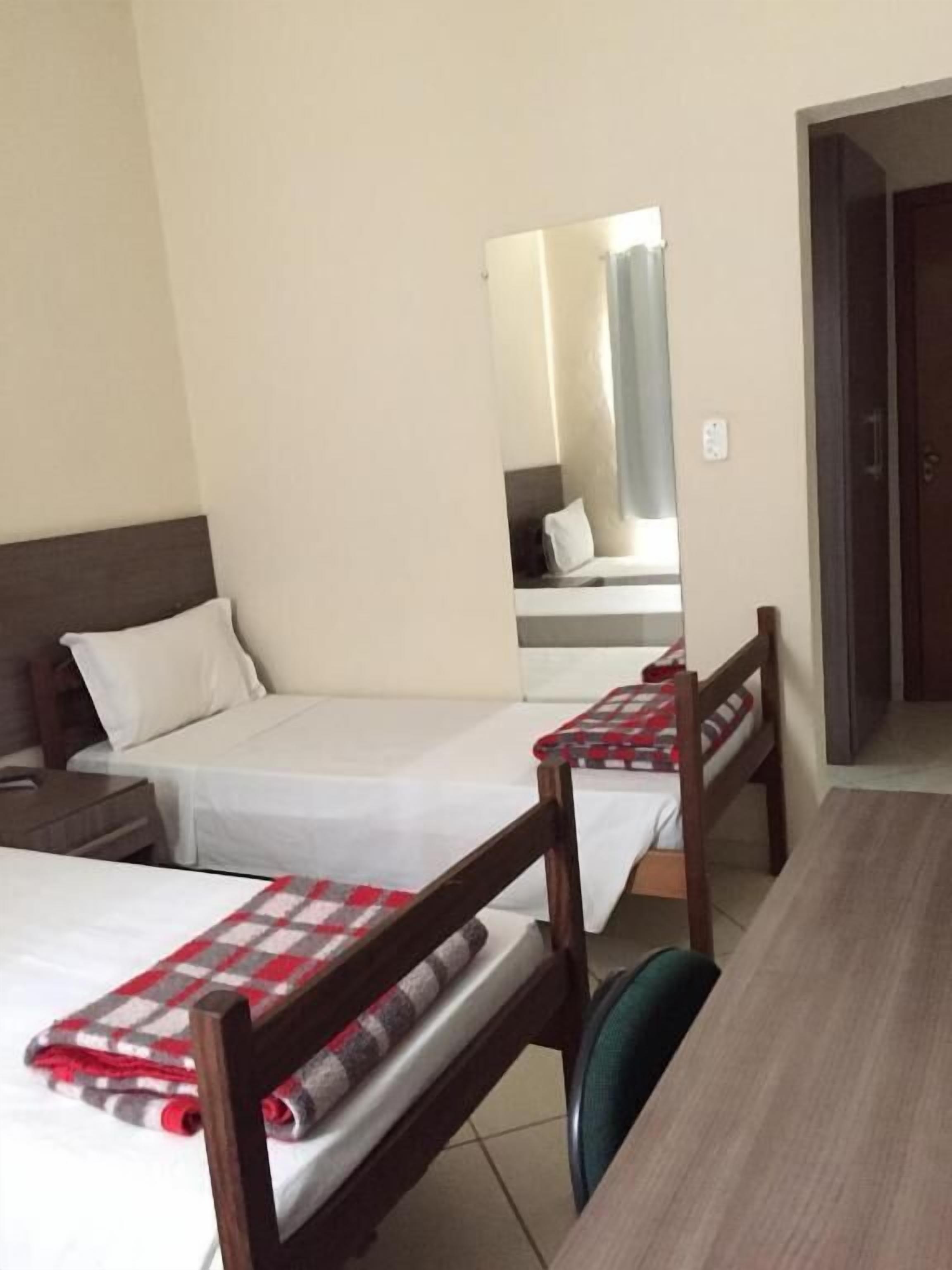 Quarto de hotel com duas camas de solteiro, cabeceira de madeira, uma escrivaninha e uma cadeira.