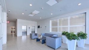 Uma área de espera moderna com sofá, cadeiras, mesa de centro e plantas em vasos.