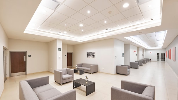 Um hall espaçoso com várias áreas de estar, uma mesa de centro e um pé-direito alto com iluminação embutida.