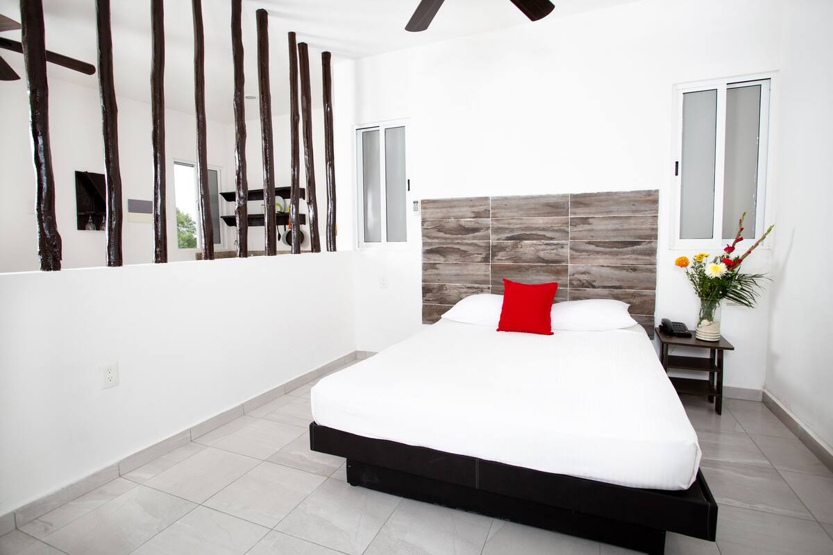 Quarto moderno com cama grande, cabeceira de madeira e mesinha de cabeceira com uma planta.