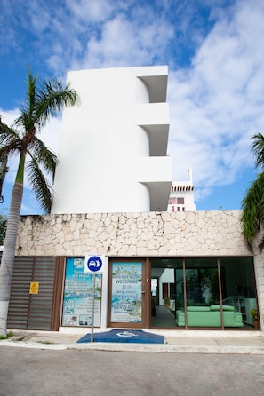 Hotel com design moderno, apresentando fachada de pedra e um edifício branco grande ao fundo.