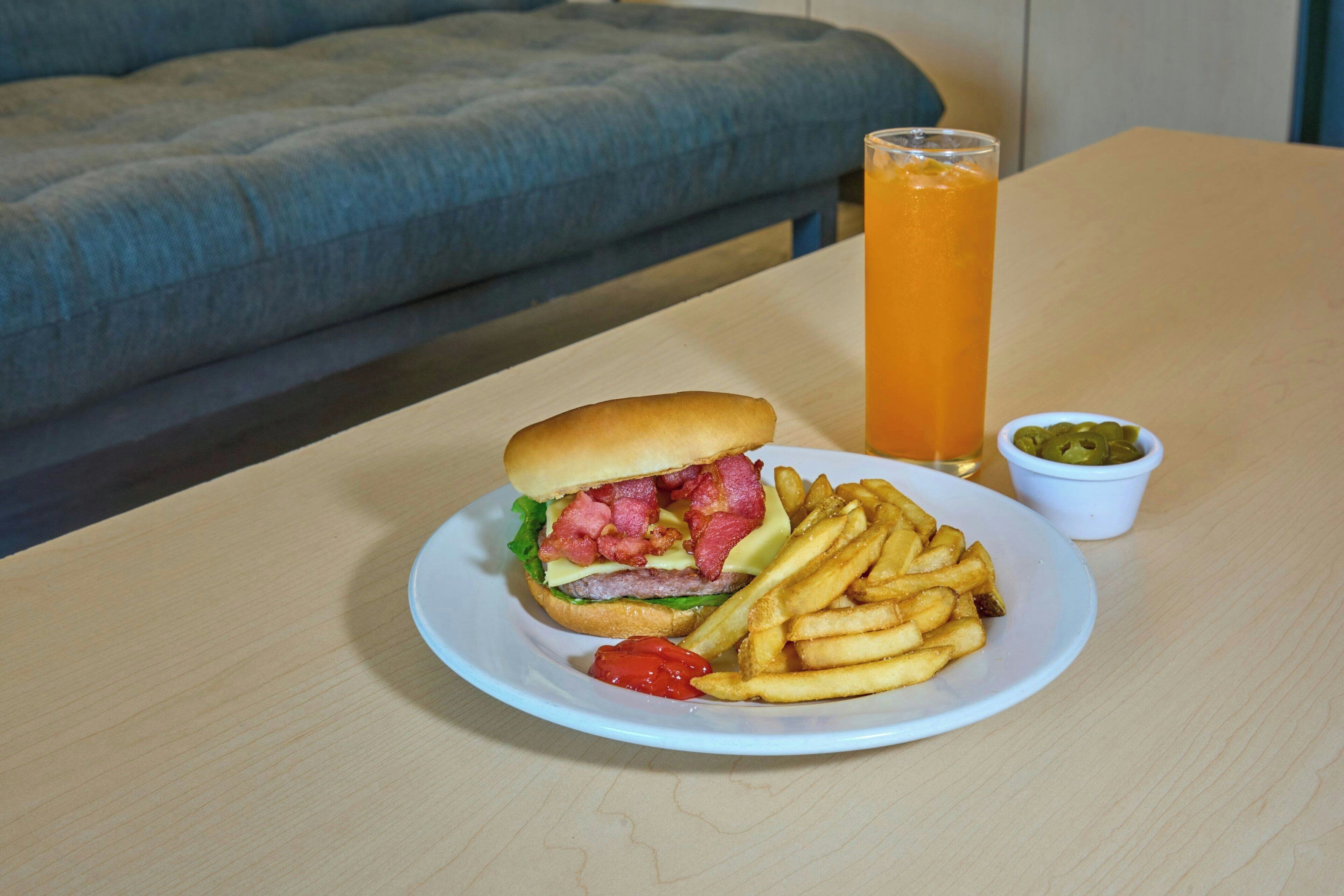 Um prato com um hambúrguer, batatas fritas e uma bebida sobre uma mesa.