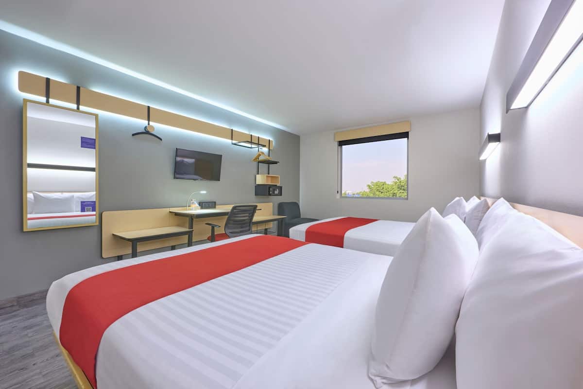 Quarto de hotel com duas camas, uma escrivaninha, uma cadeira, uma televisão e uma janela.