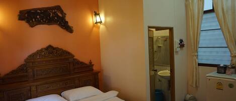 Quarto de hotel com cabeceira de madeira, cama com roupa de cama branca, luminária fixada na parede, espelho e janela com cortinas.