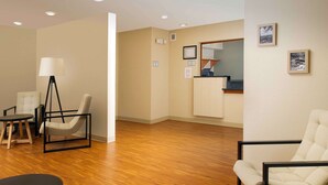 Quarto de hotel com piso de madeira, uma escrivaninha com abajur, duas cadeiras, um espelho e quadros nas paredes.