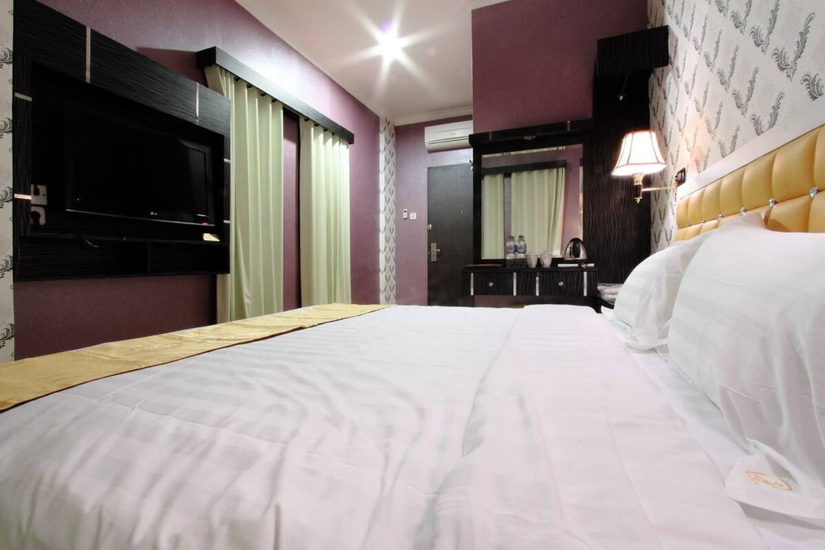 Quarto de hotel com uma cama grande, televisão de tela plana na parede, penteadeira com espelho e luminária de cabeceira.