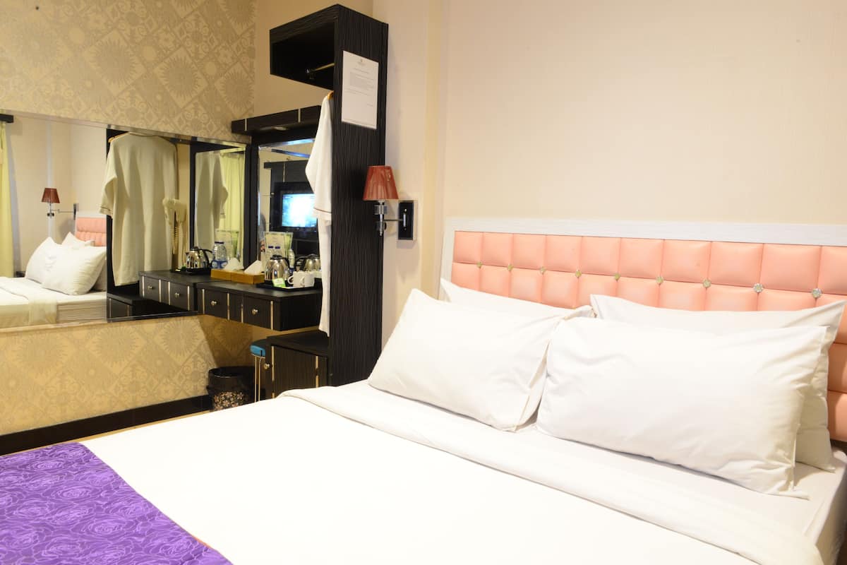 Quarto de hotel com uma cama grande, uma toucador com espelho e uma televisão.