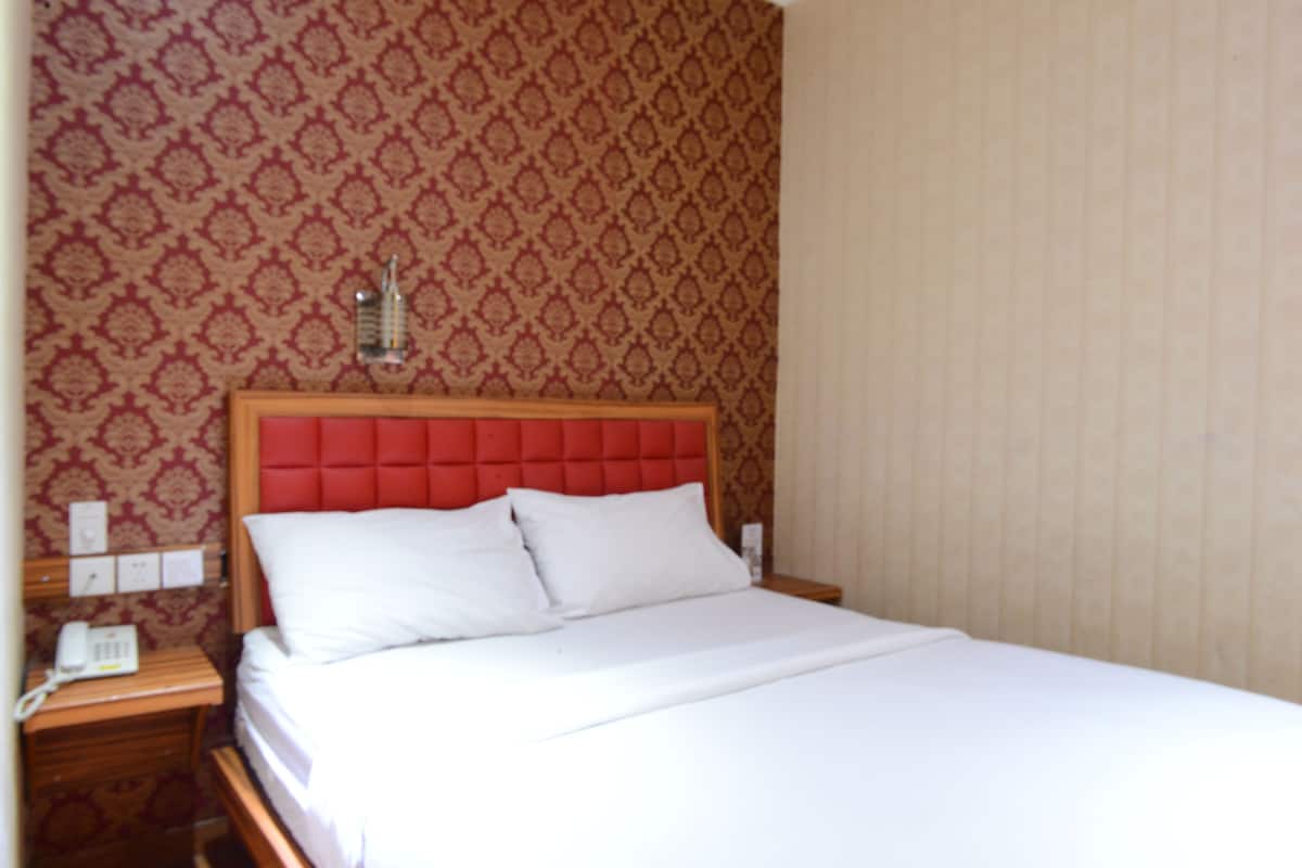 Quarto de hotel com cabeceira vermelha, roupa de cama branca, telefone na mesa de cabeceira e papel de parede estampado.