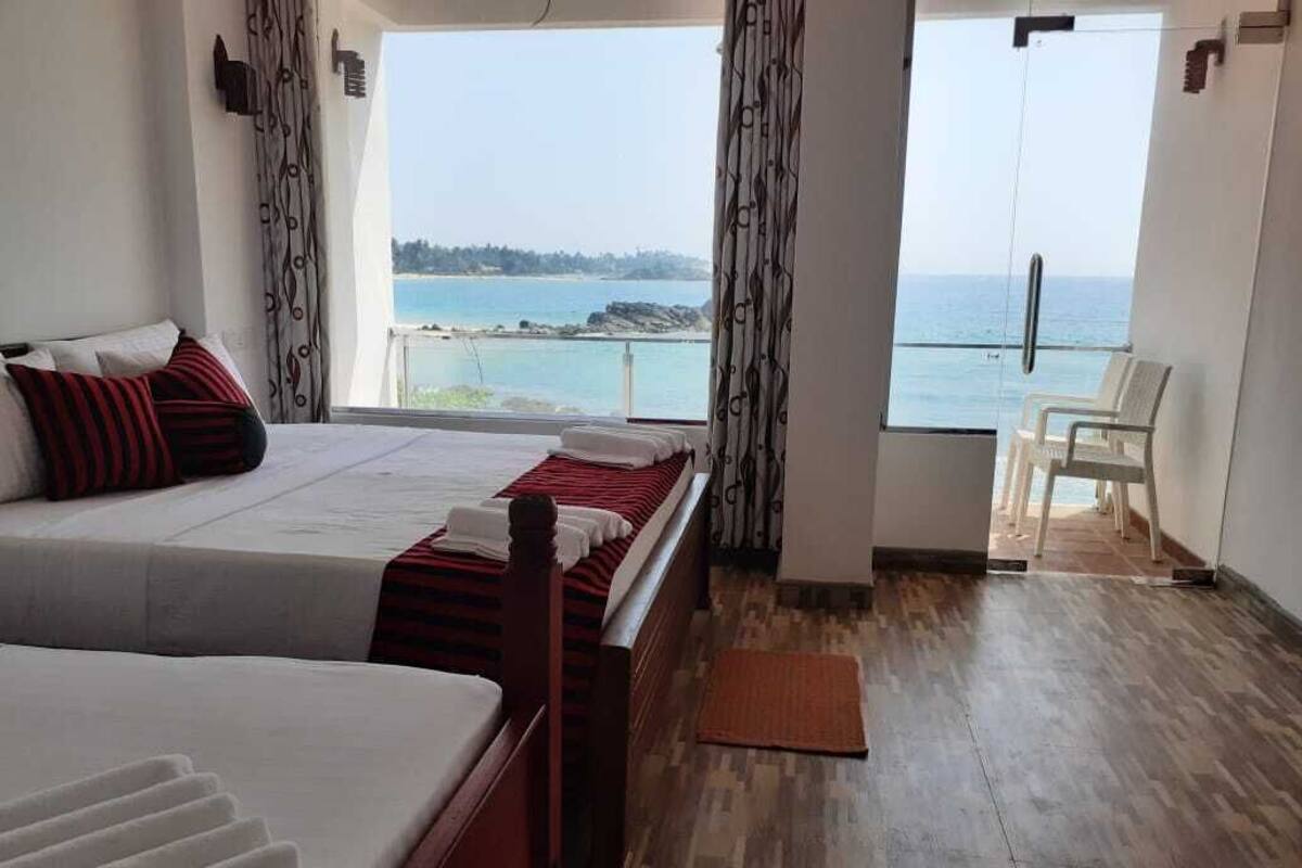 Quarto de hotel com duas camas, vista para o mar e varanda com uma cadeira.
