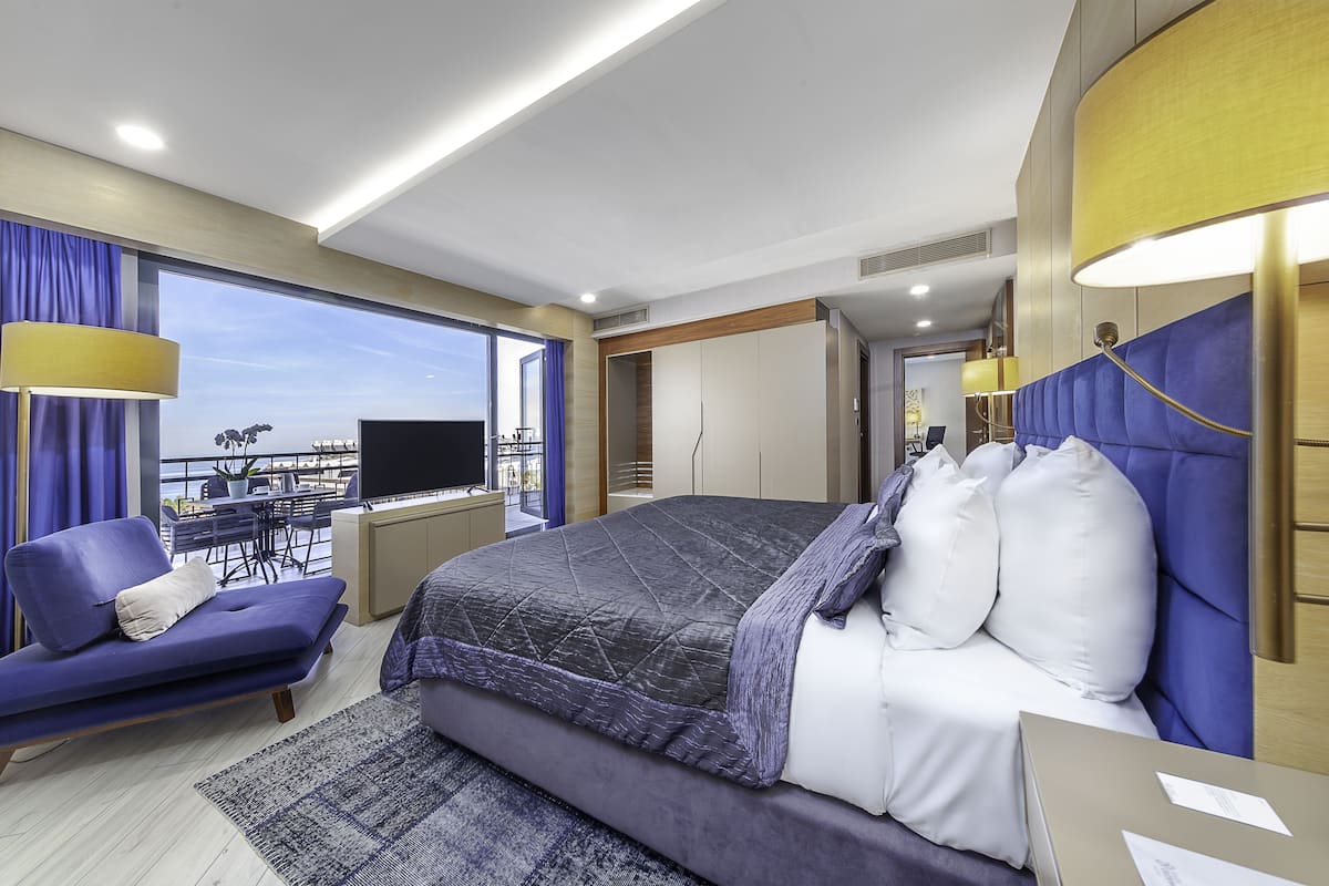 Quarto de hotel moderno com uma cama grande, um sofá, uma escrivaninha com televisão de tela plana e uma varanda com vista para a cidade.