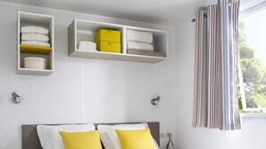 Cama bem arrumada com roupa de cama branca e duas almofadas amarelas, mesa de cabeceira com abajur, e bandeja com maçãs e xícaras sobre a cama.