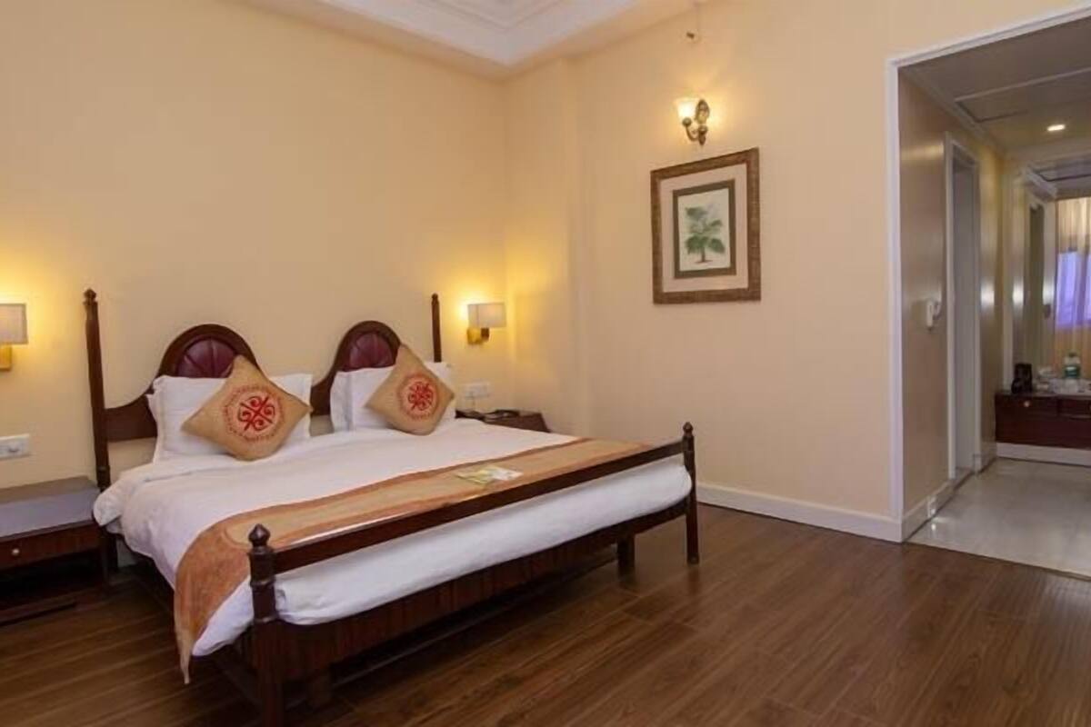 Quarto de hotel com cama de madeira, duas luminárias de cabeceira, mesa de apoio e um quadro na parede.