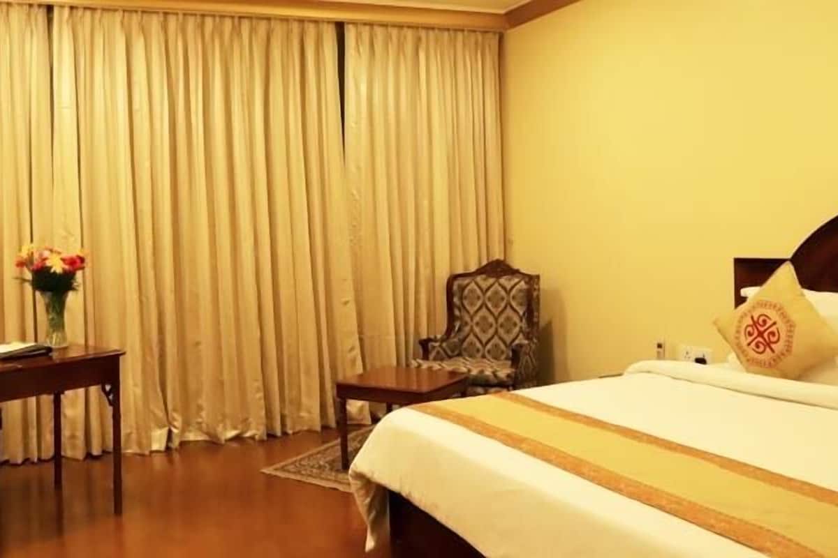 Quarto de hotel com cama, escrivaninha com luminária, cadeira e cortinas.