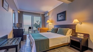 Quarto de hotel com cama grande, mesas de cabeceira, escrivaninha, cadeira e vista para o exterior.