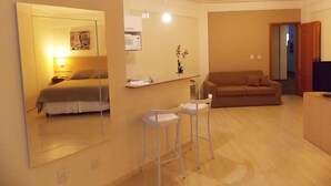 Uma sala de estar moderna com sofá, uma área de jantar com mesa e cadeiras, e um espelho grande refletindo o ambiente.