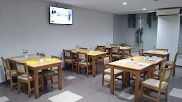 Uma sala de conferência com várias mesas e cadeiras, uma tela fixada na parede e um ar condicionado.
