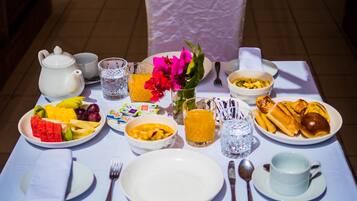 Mesa de café da manhã com diversos pratos, incluindo frutas, pão e bebidas.