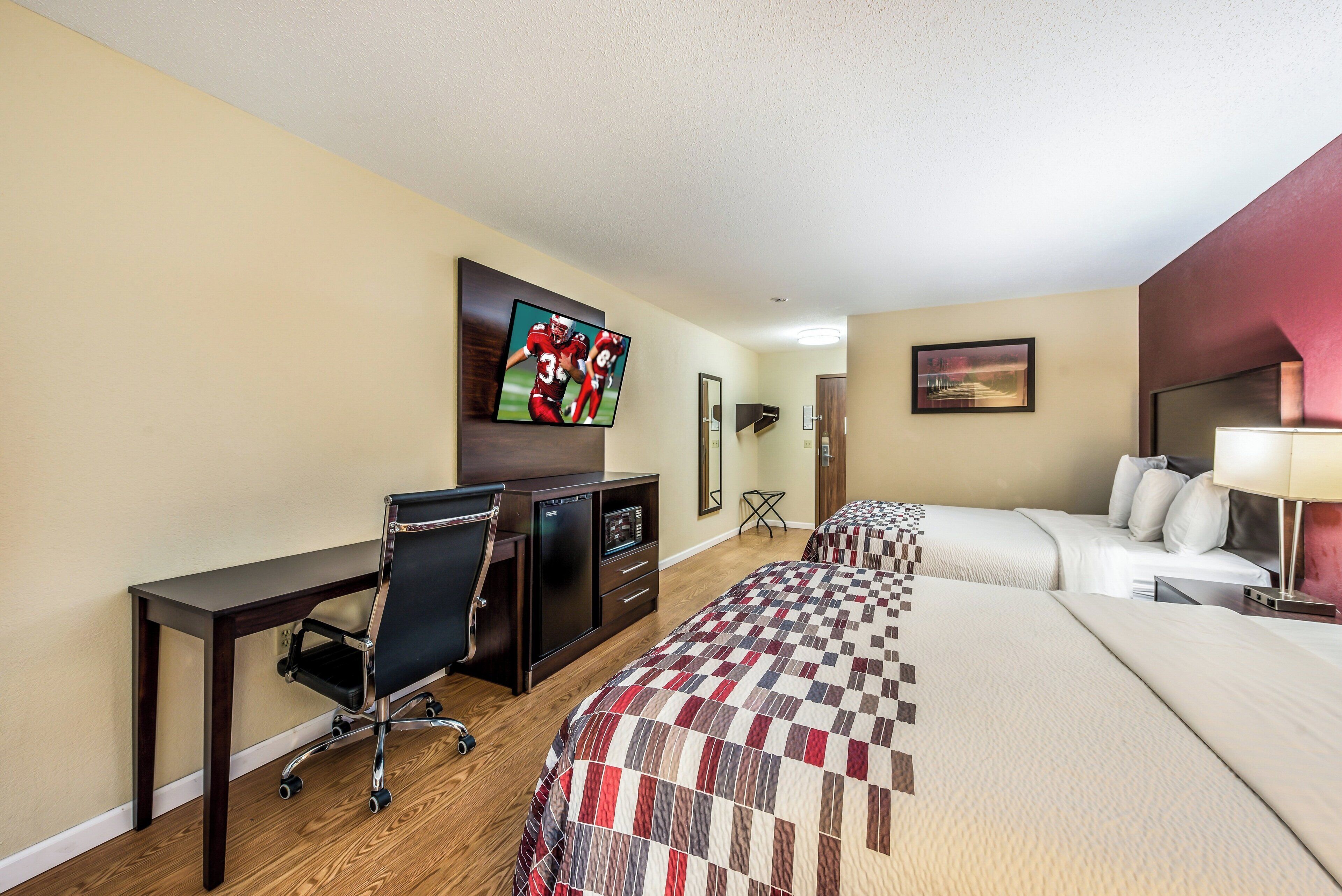 Quarto de hotel com escrivaninha, cadeira, duas camas, televisão e obras de arte nas paredes.