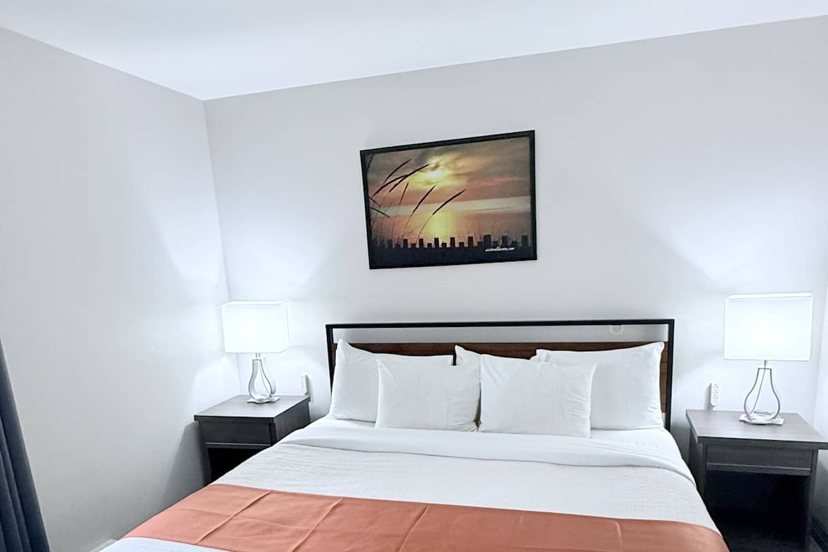 Quarto de hotel com uma cama grande, duas mesas de cabeceira com luminárias, um quadro com vista para a cidade e design moderno.