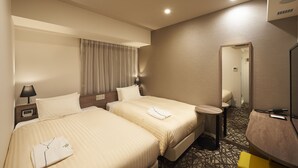 Quarto de hotel com duas camas, uma mesa de cabeceira com abajur, uma mesinha redonda e um espelho.