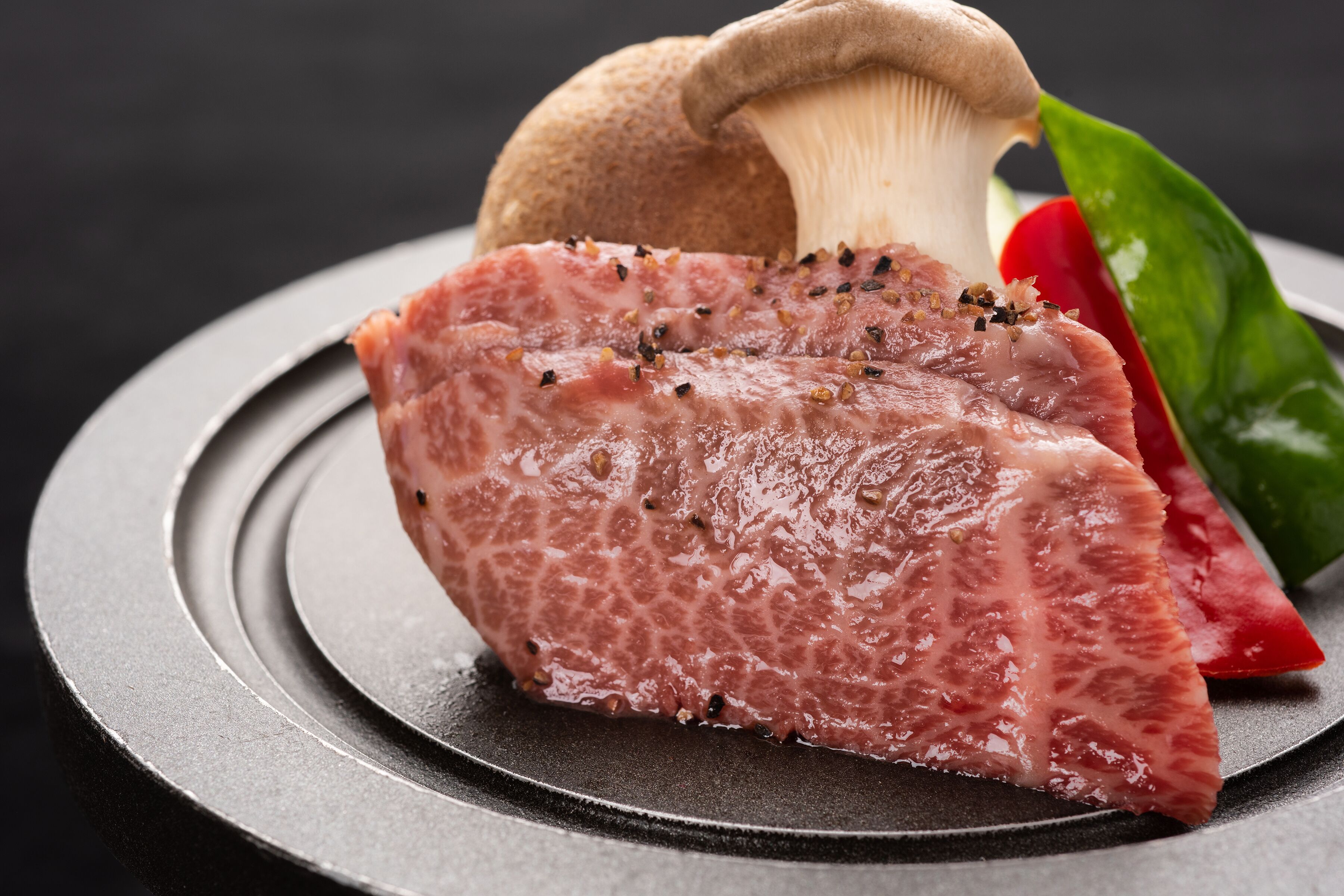 Um prato com uma fatia de carne, um cogumelo e um pimentão vermelho.