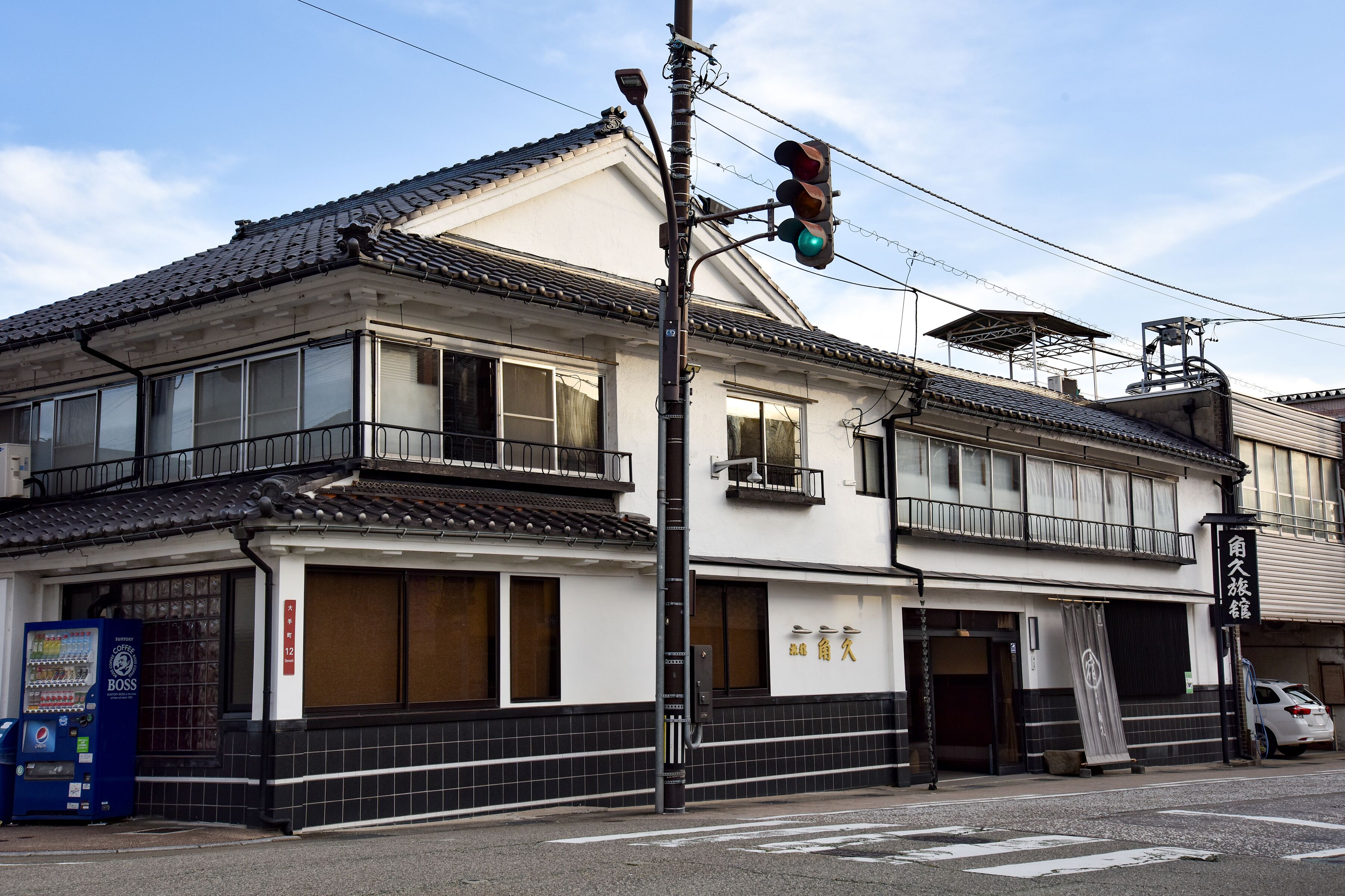 Um edifício tradicional japonês com telhado telhado, janelas grandes e um distribuidor automático na calçada.