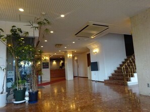 Um hall amplo com piso de mármore polido, escada com grades douradas e plantas em vasos.